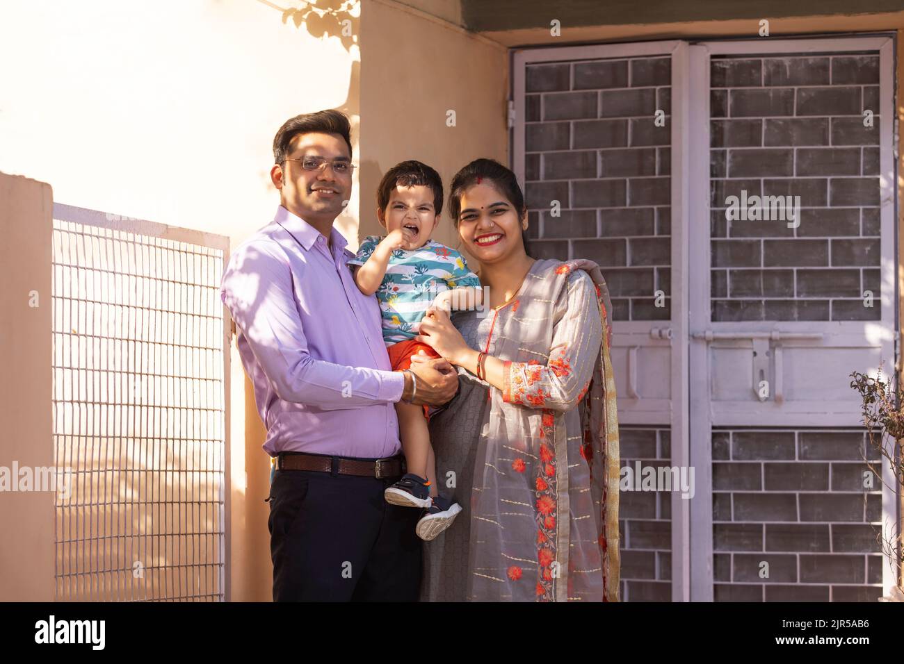 Portrait of happy couple with their child standing in front of entrance ...