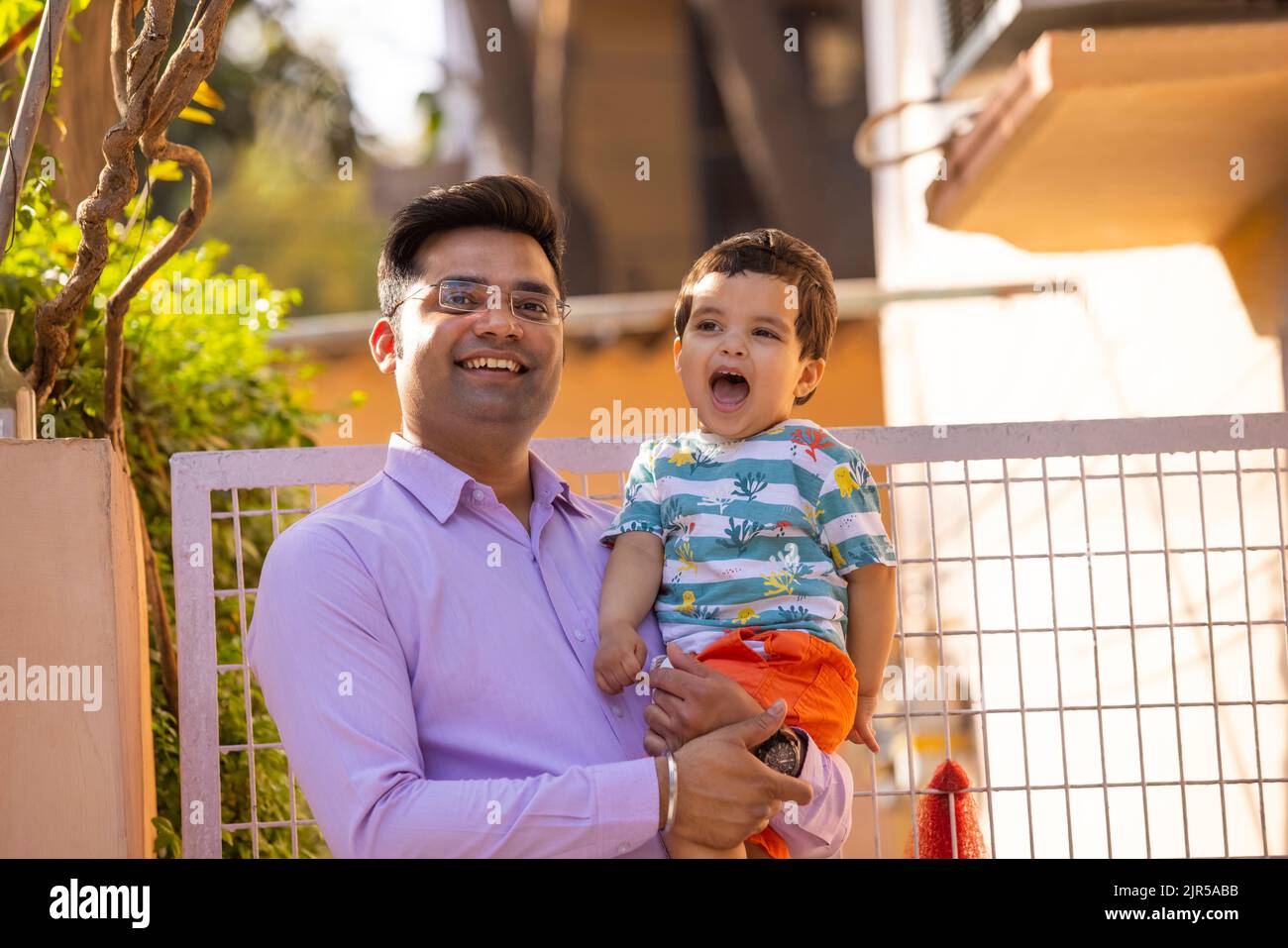 Portrait of happy father with his their child standing in front of gate ...
