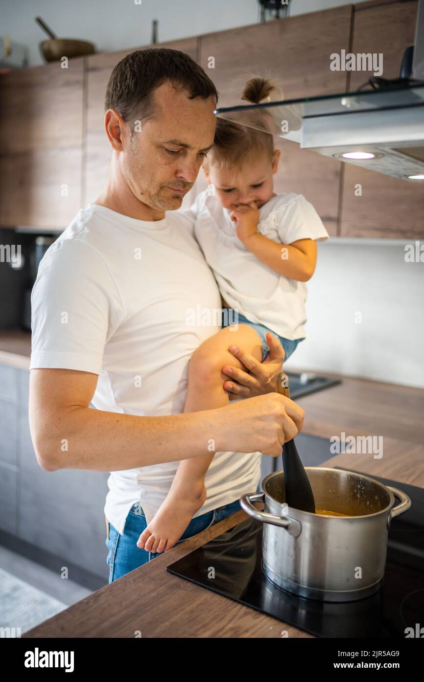 Father with his daughter on his hands cooking soup together in modern ...
