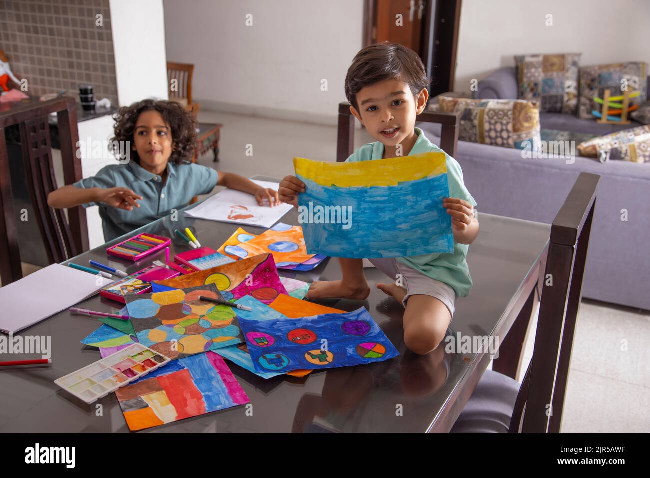 Younger brother holding up a colourful painting while elder brother ...