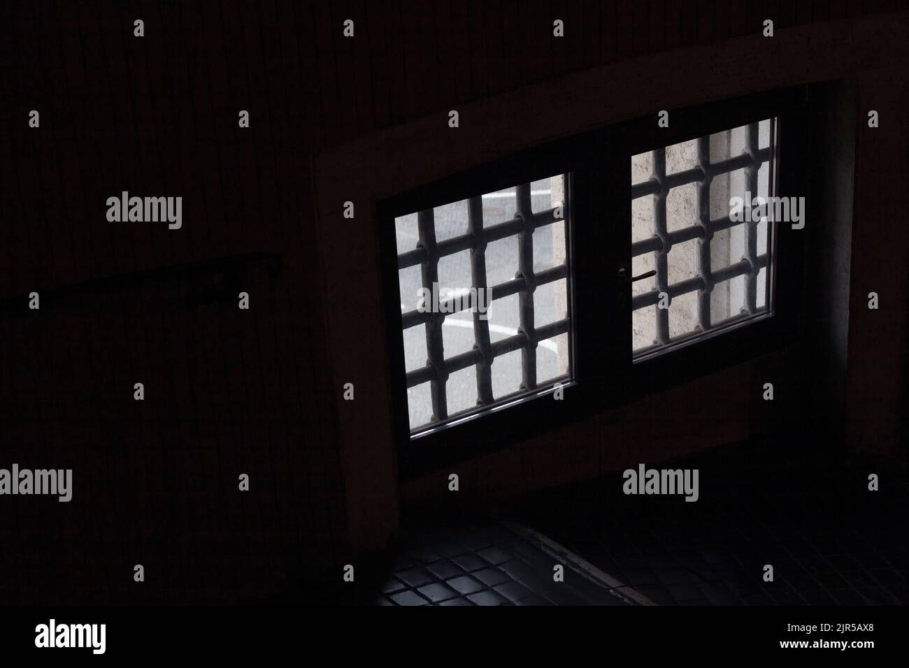 Dark room with window in grate . Inside prison cell . Light high ...