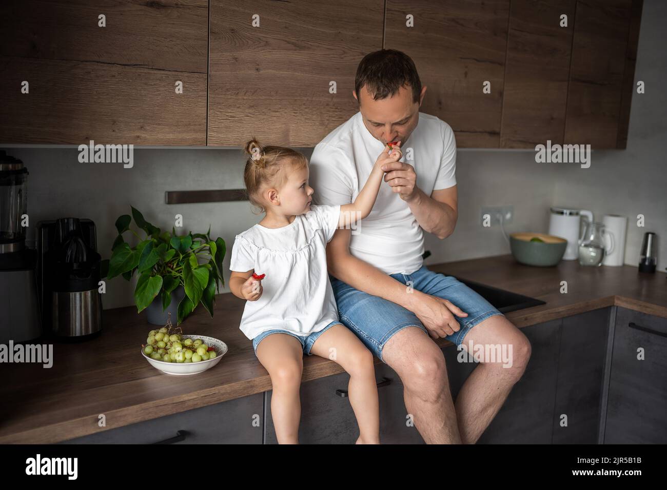 Cute little girl and her handsome dad are eating fruit in modern ...