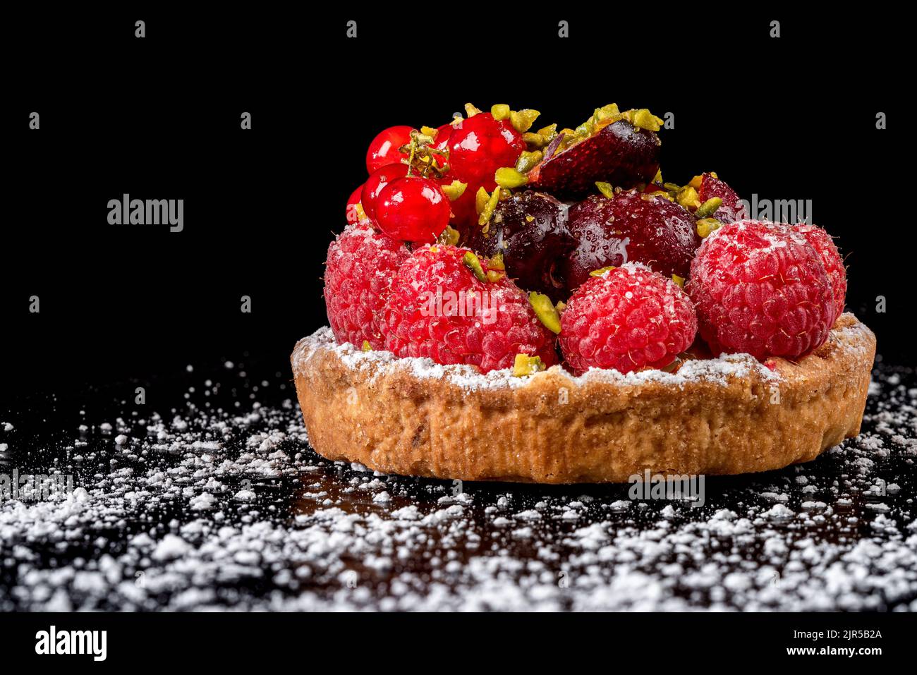 A very nice fruit tart on a black background. Powdered sugar is placed ...