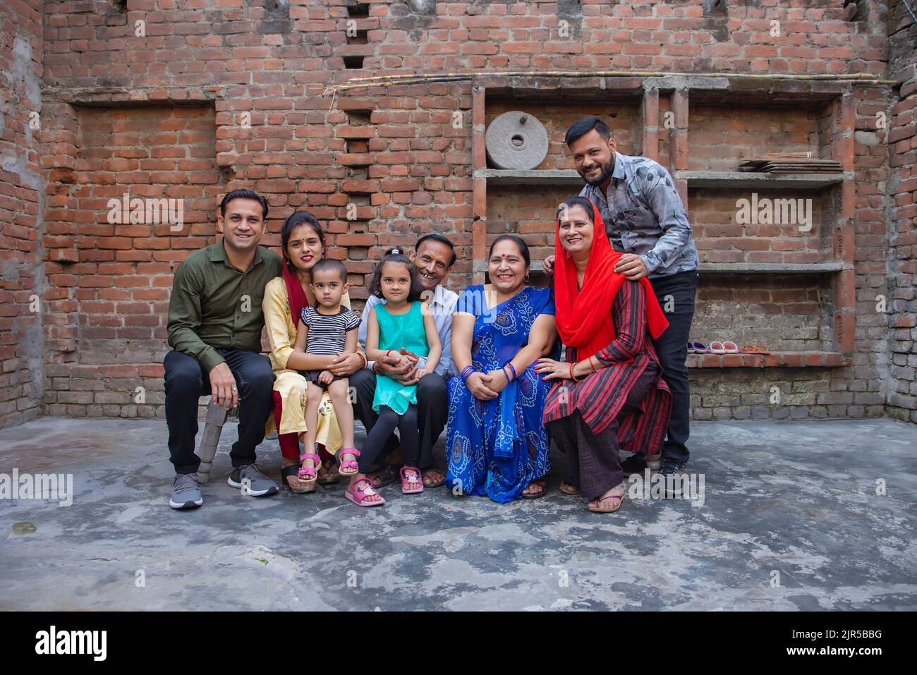 Portrait of lower middle class family sitting together on cot in the ...