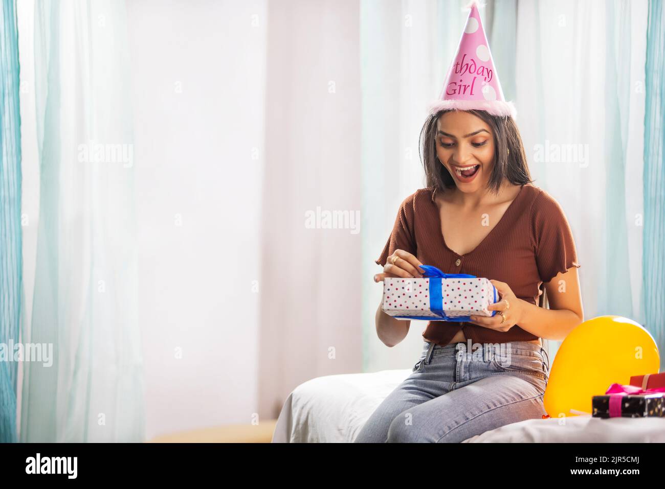 Excited young woman opening birthday gift while sitting on bed Stock ...