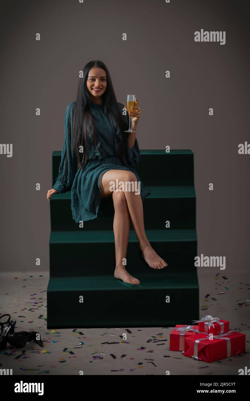 Cheerful young lady in ceremonial outfit sitting on stair with holding ...