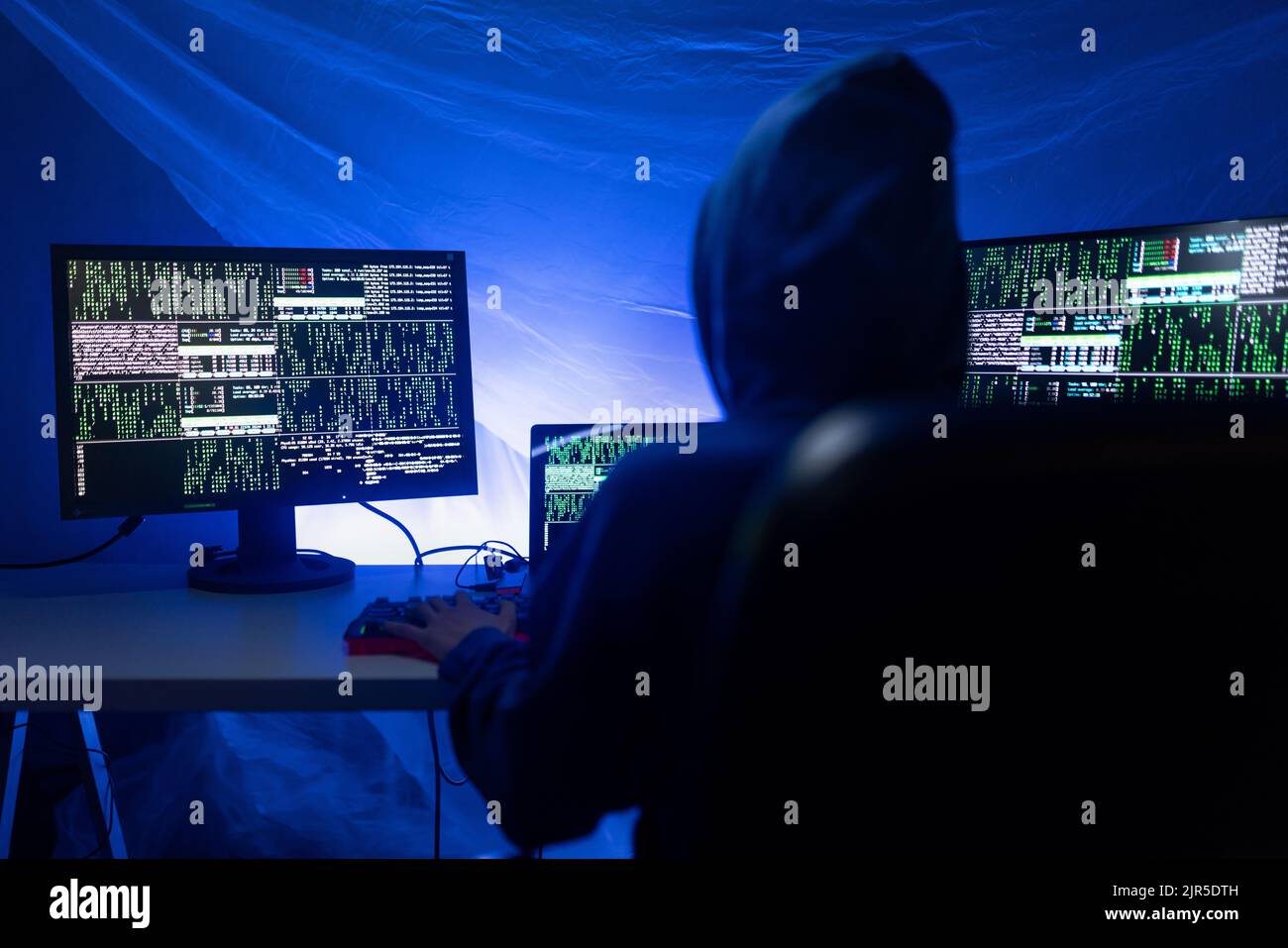 Rear view od hooded hacker by computer in the dark room at night ...