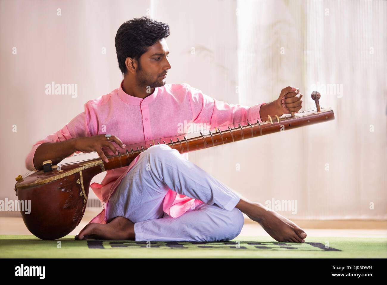 Young male musician tuning his sitar while sitting in living room Stock ...