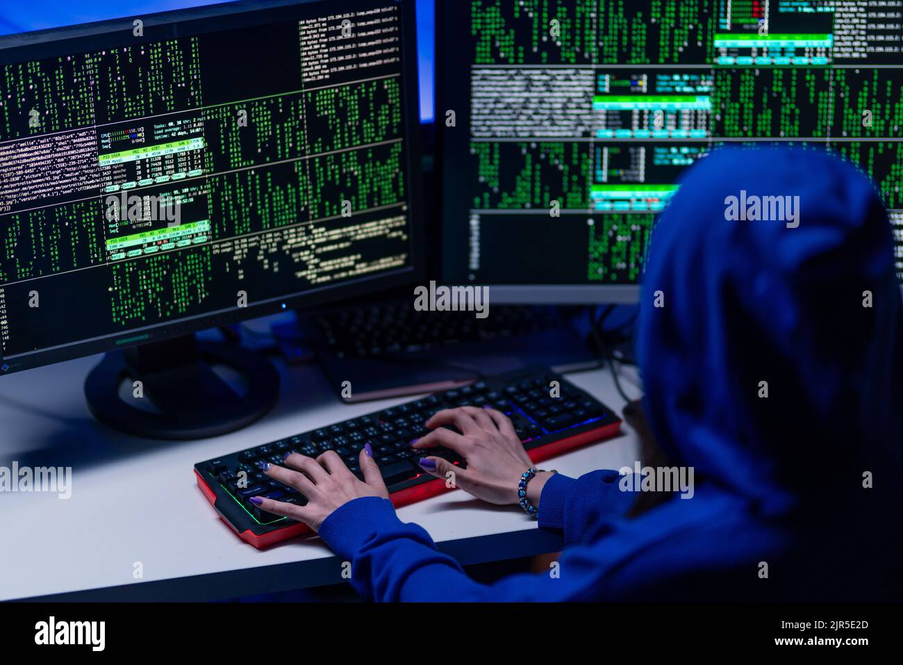 Rear view od hooded hacker by computer in the dark room at night ...