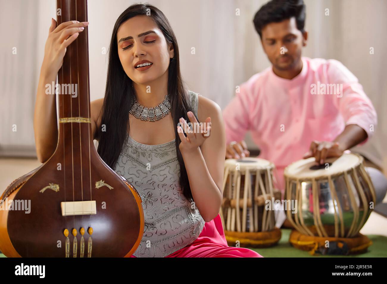 Close-up view of a young woman playing Tanpura and a man accompanying ...