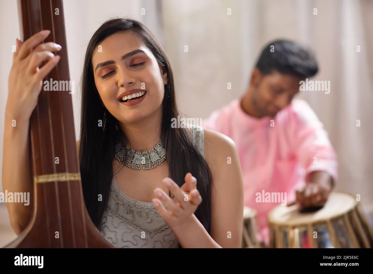 Close-up view of a young woman playing Tanpura and a man accompanying ...