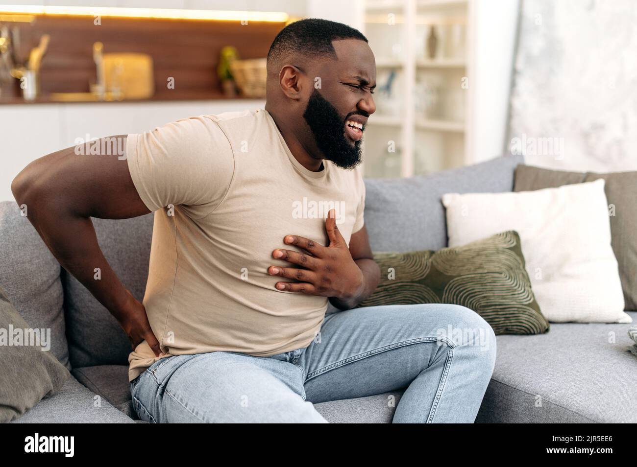 Upset african american young man, in casual wear, sitting on sofa in ...