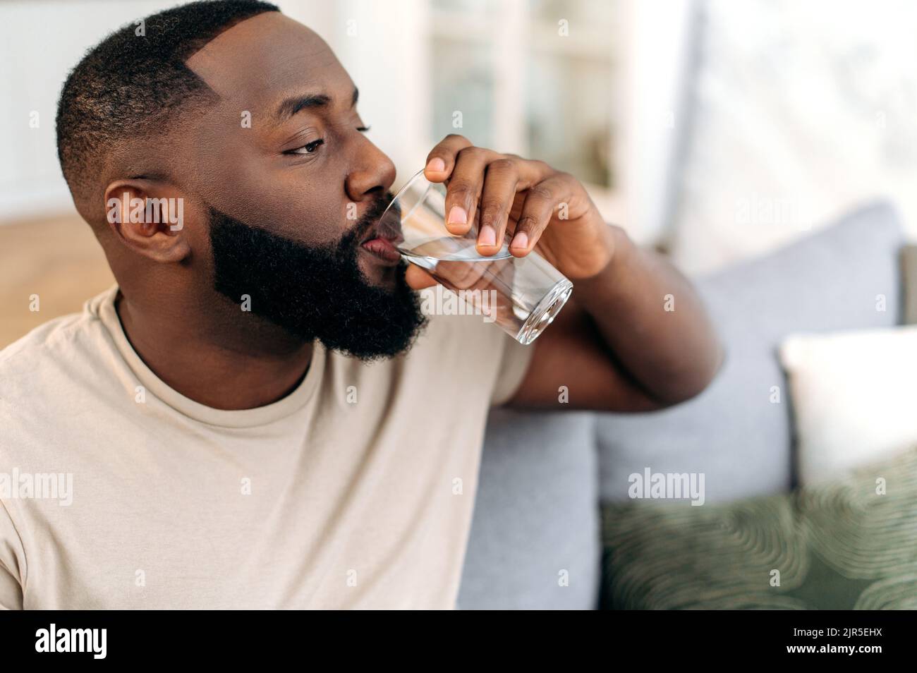 Close-up of african american man, drinks a glass of clean water with ...