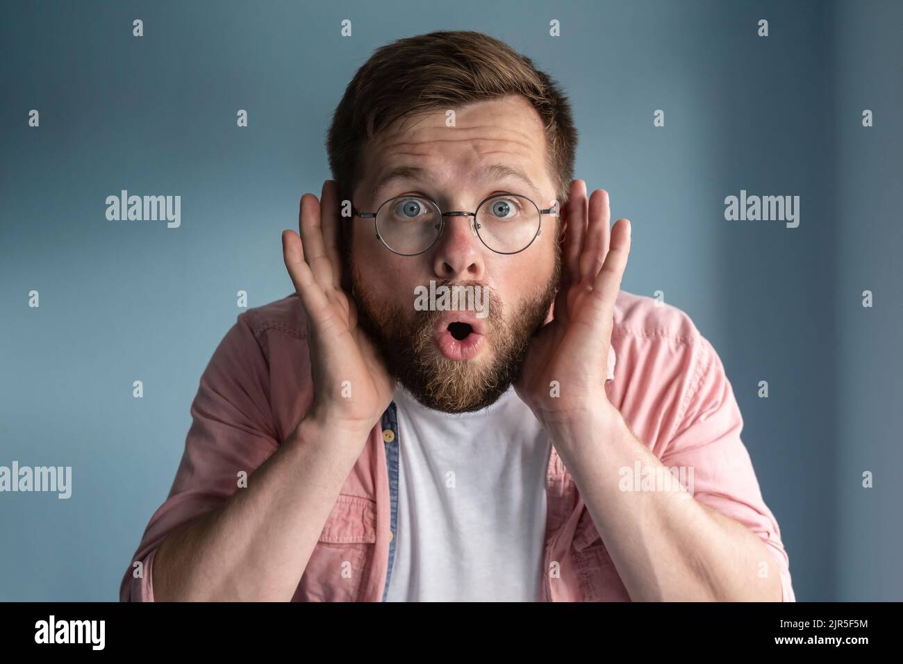 Man with glasses eavesdrops with his hands to ears, he opened mouth in ...