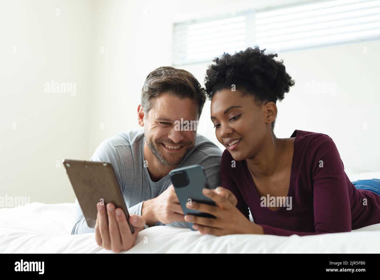 Image of happy diverse couple using smartphone and tablet and lying in bed Stock Photo - Alamy