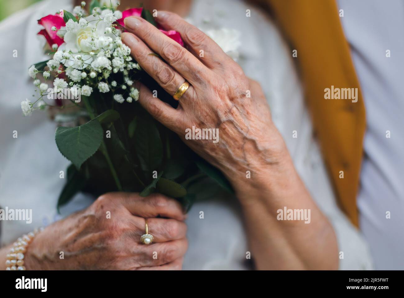 Close-up of senior hands with wedding bouquet and wedding rings during ...