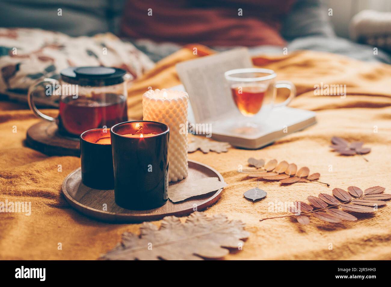 Cozy bed with cup of tea, candles and open book. Concept of autumn cozy ...