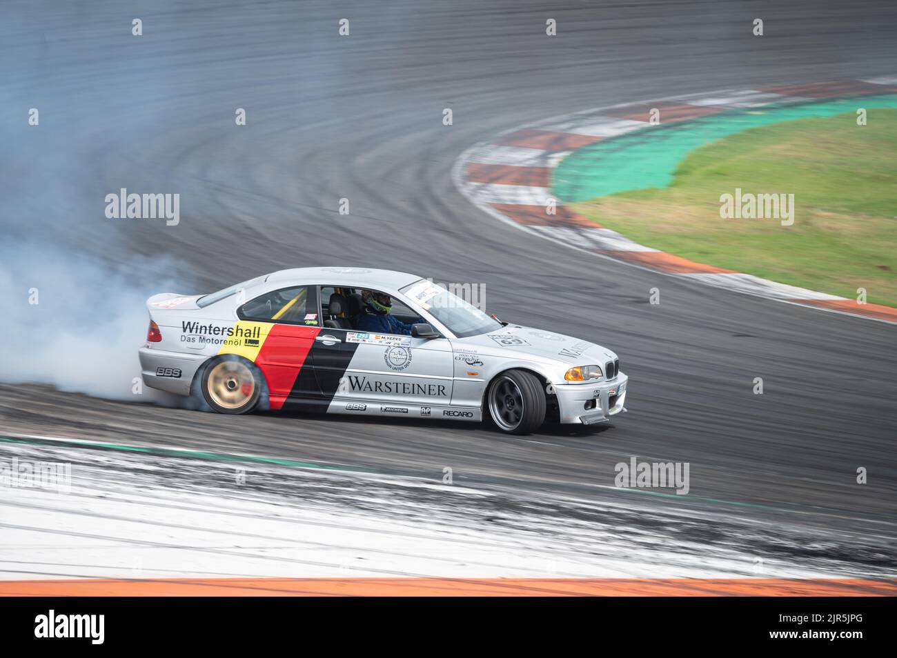 A gray BMW E46 with the German flag colors producing smoke on a trail ...