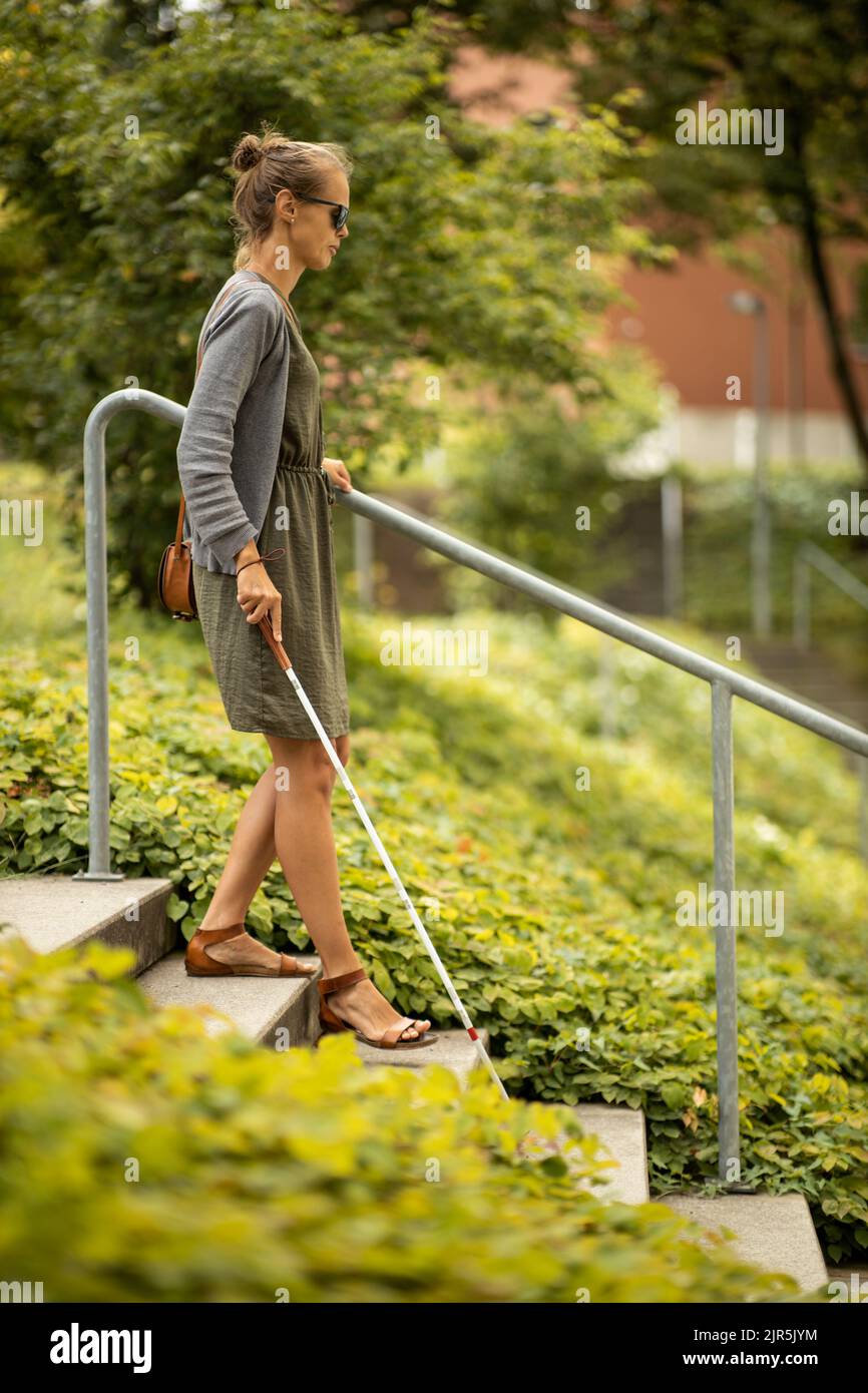 Blind woman walking on city streets, using her white cane to navigate ...
