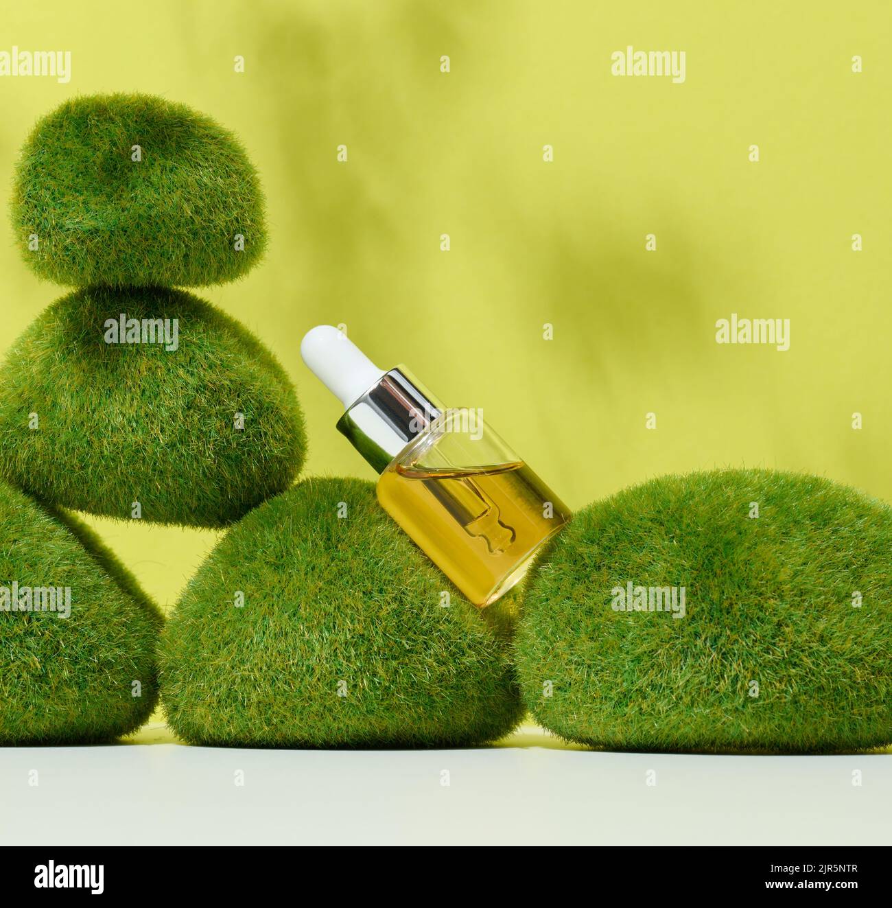 Glass transparent bottle with pipette and yellow oil on green moss ...