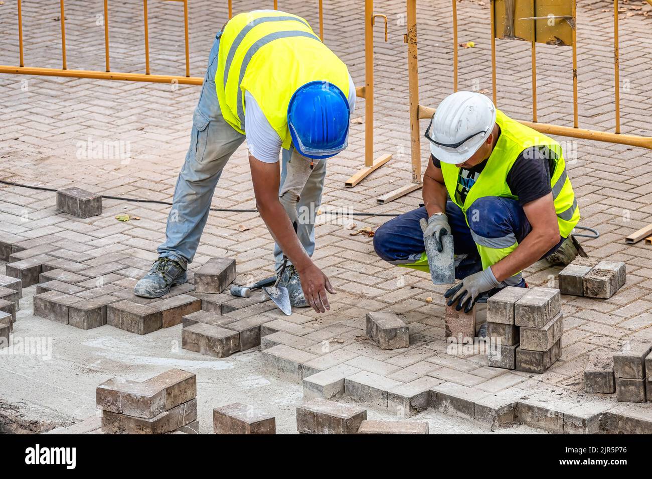 Two bricklayers working in the repair of sidewalk in the Port Vell or ...