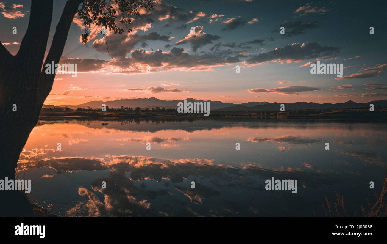 A colorful sunset reflected on the water with trees and mountains in ...