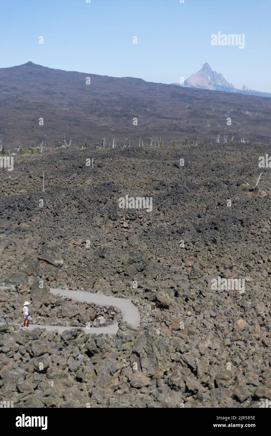 A person walking along a trail through the lava flow, with a peak in ...