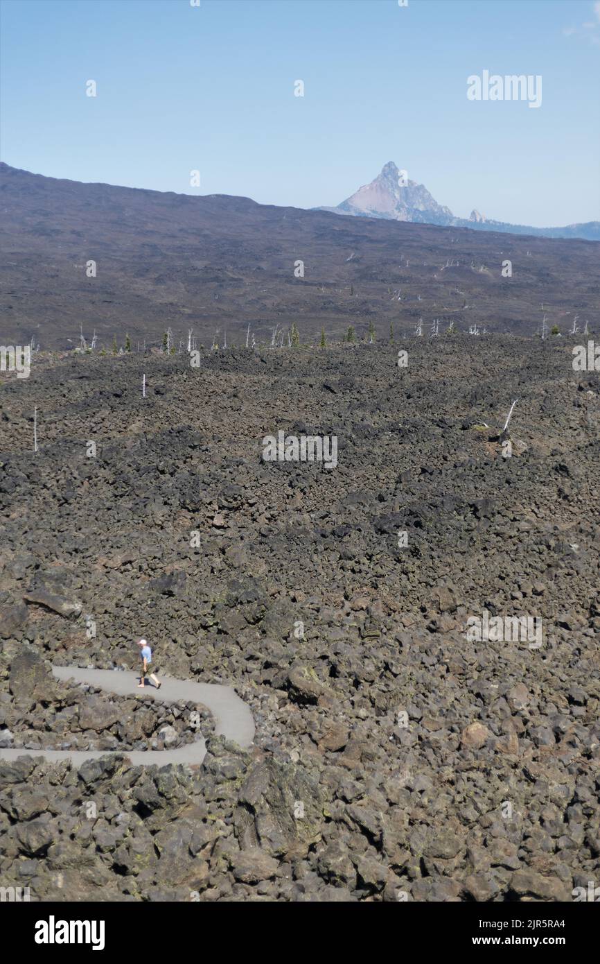 A person walking along a trail through the lava flow, with a peak in ...