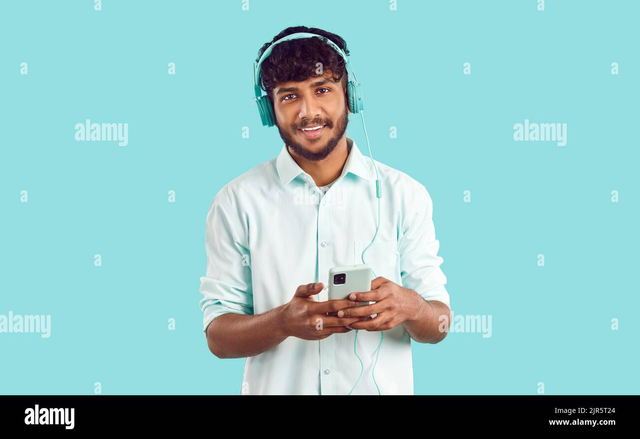 Portrait of happy young Indian man in headphones and with smartphone on ...