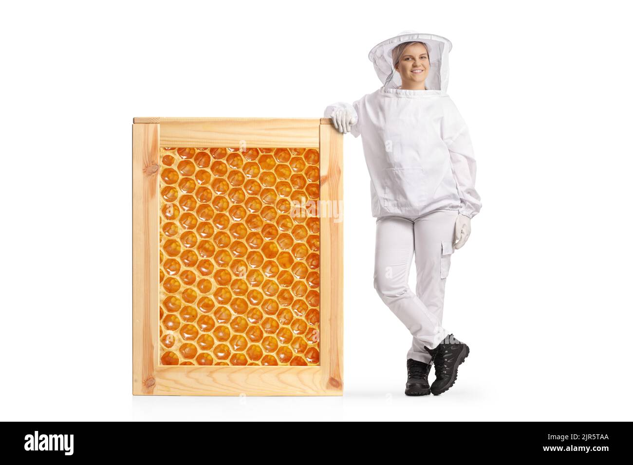 Young female bee keeper in a uniform leaning on a big honeycomb frame ...