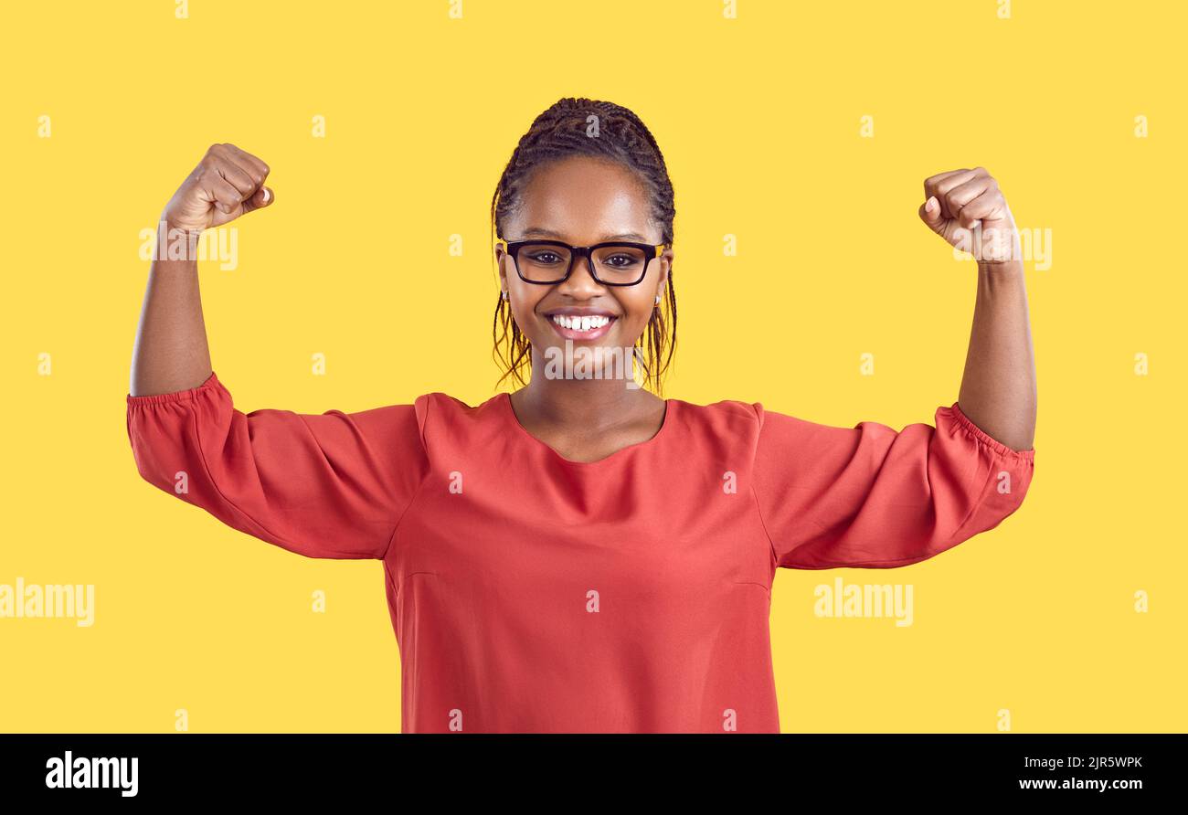 Cheerful dark skinned woman showing muscles on her arms isolated on ...