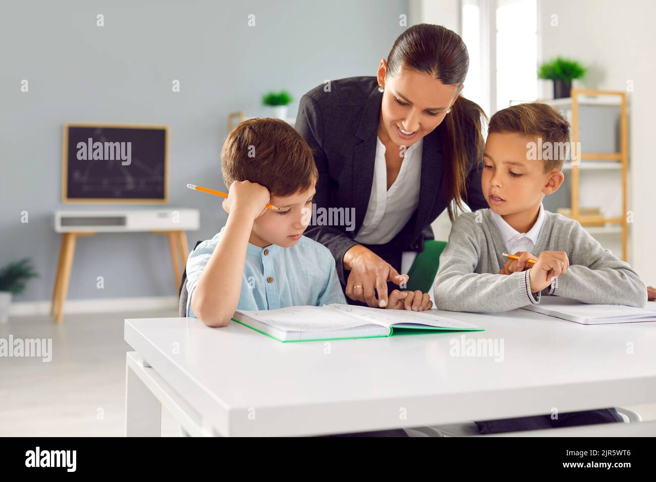 Caring female teacher helps small students learn to read and explains ...