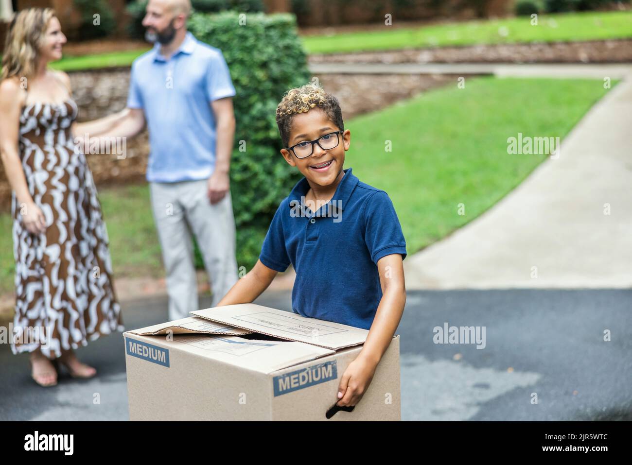 A little boy holding a moving box ready to move into his new house ...
