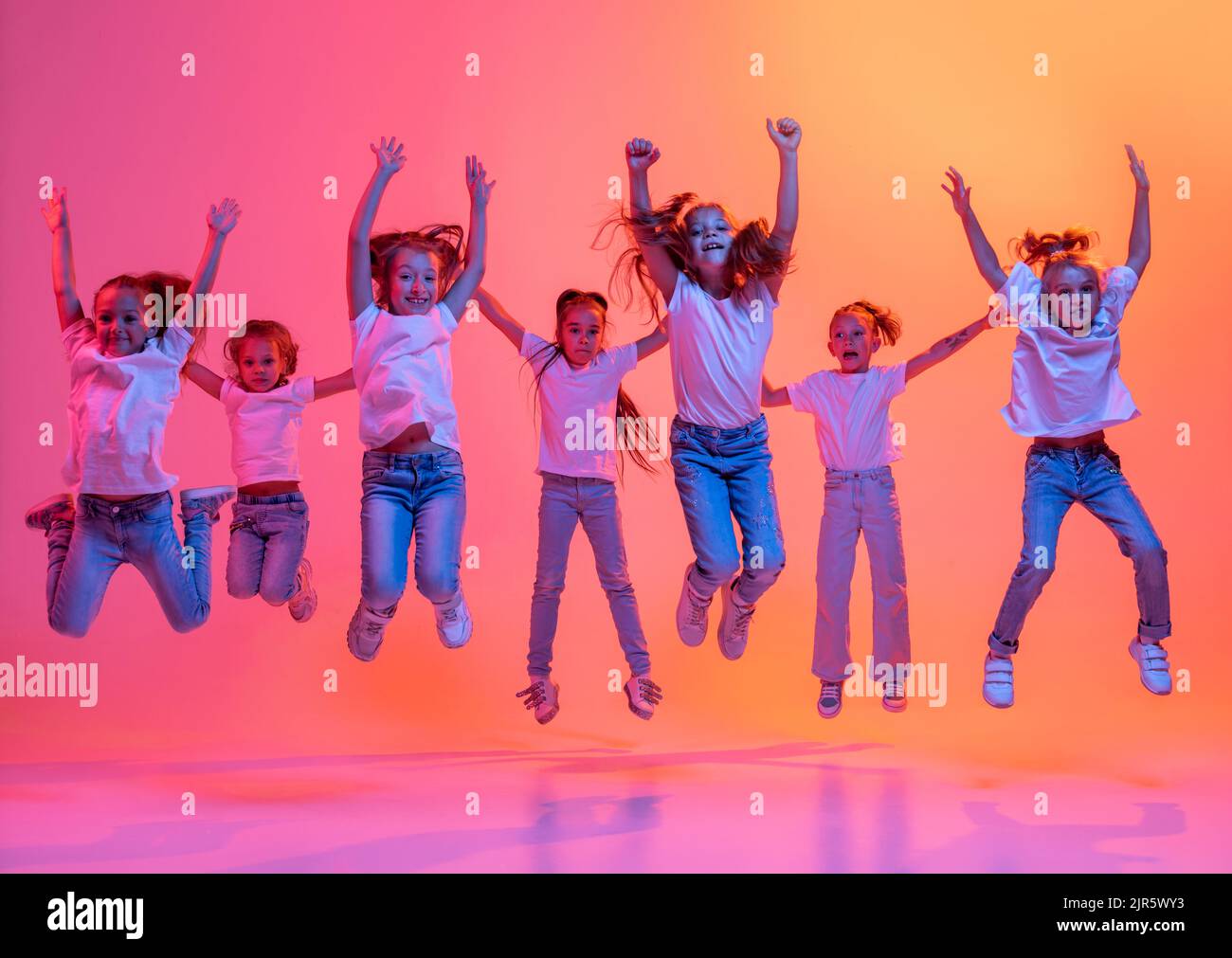 Happy kids, school age girls in white t-shirts and jeans jumping ...