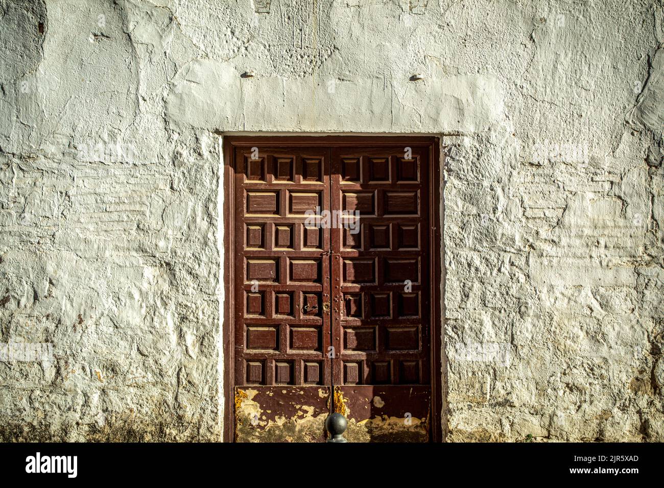 Old and worn maroon double wooden door with a lock on a whitewashed ...