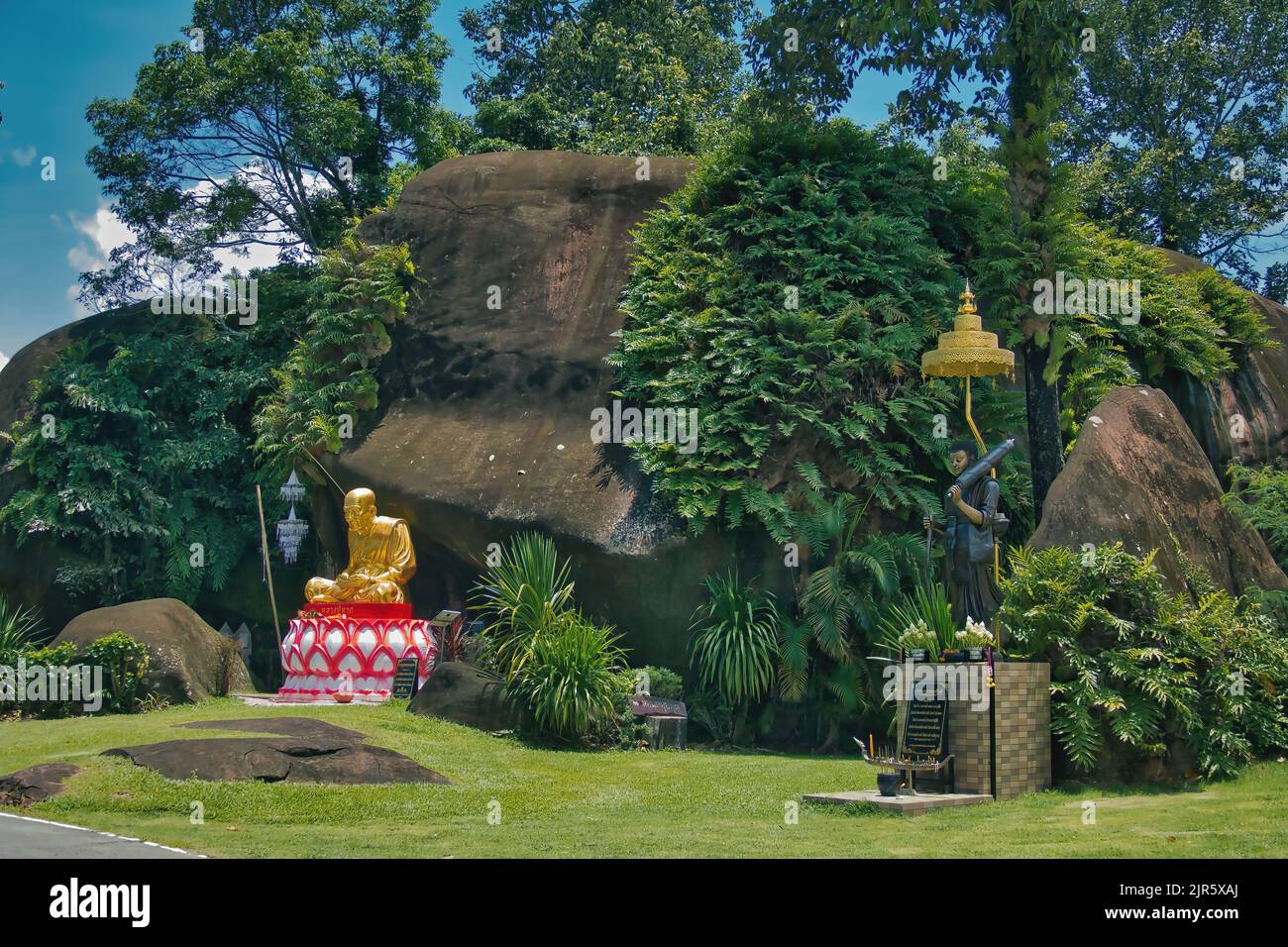 Buddhist sculptures at the foot of a giant boulder, overgrown with ...