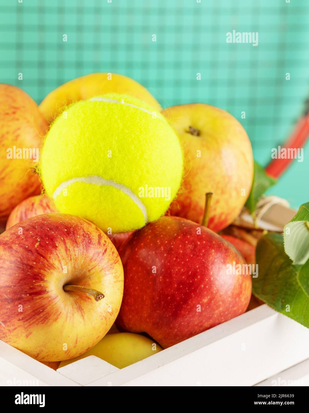 Tennis composition with yellow tennis ball, apples in a wooden box and ...