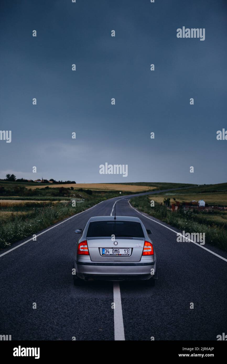 A vertical shot of a car standing on a long asphalt road on a rainy day ...