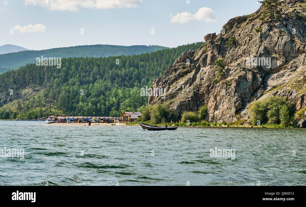 Fishing longboat with man floating along cliff near tent camp ...
