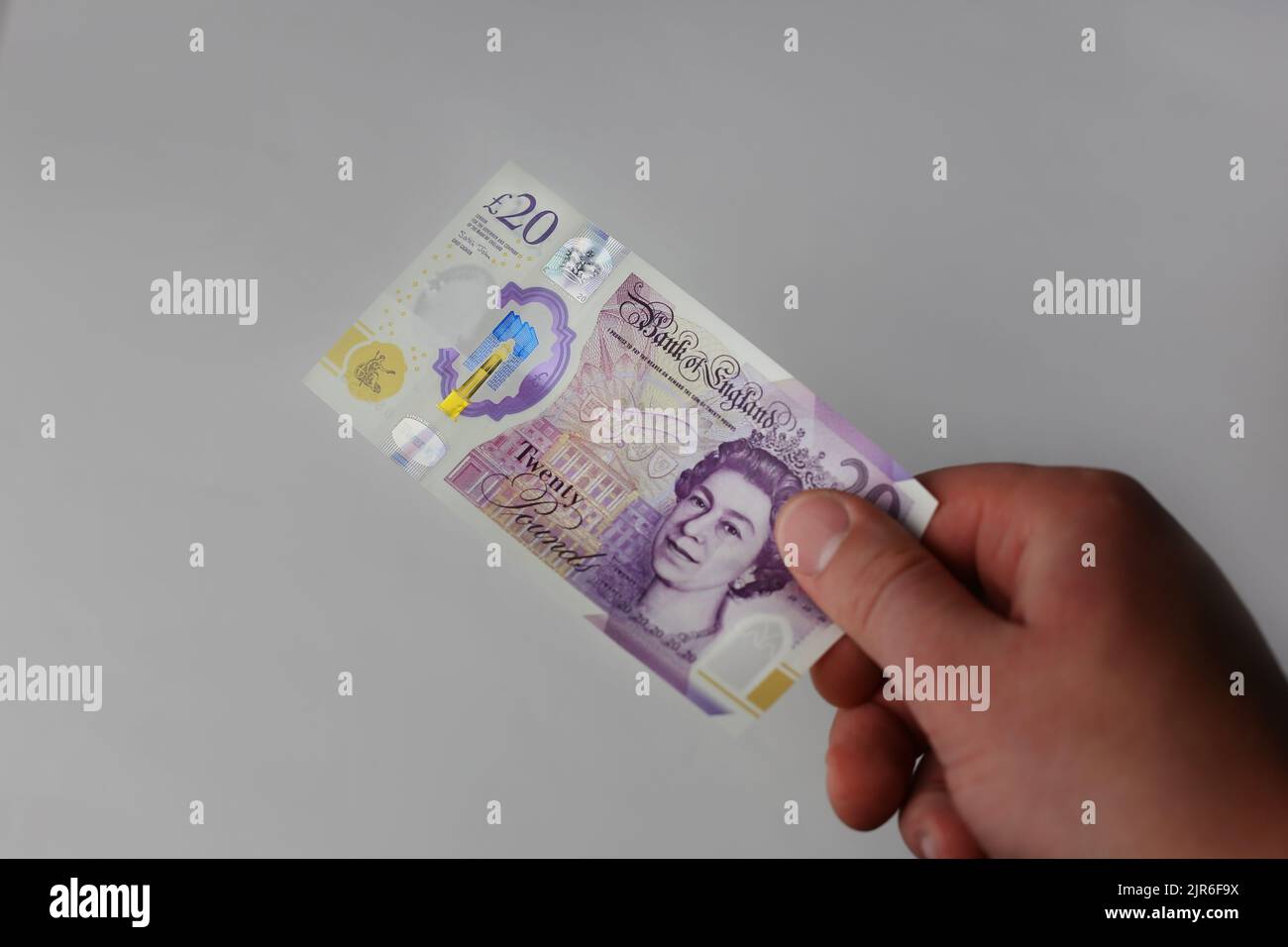 Hand giving or receiving a 20 British pound bill on a gray background ...