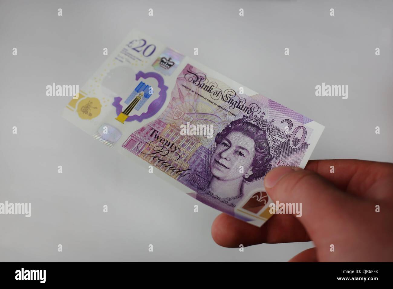 Hand giving or receiving a 20 British pound bill on a gray background ...