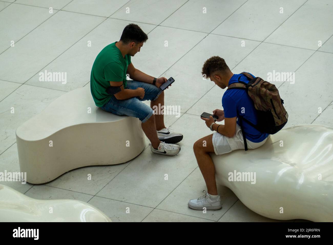 two men using cell phones sitting on benches at the Oculus in downtown ...