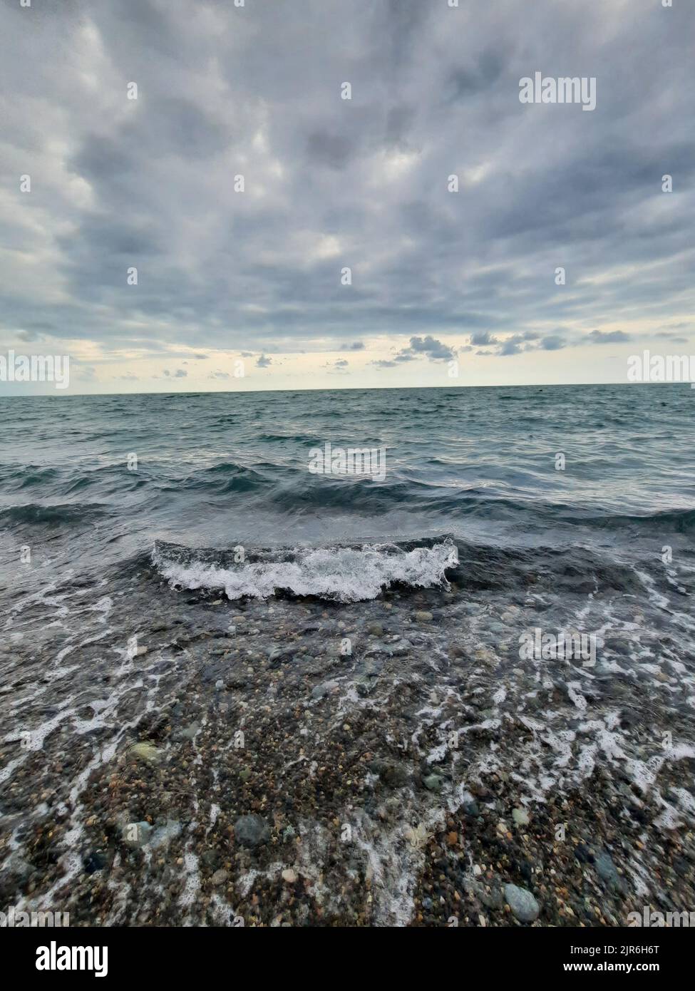 A vertical shot of a wave splashing over a pebbled coast under the ...