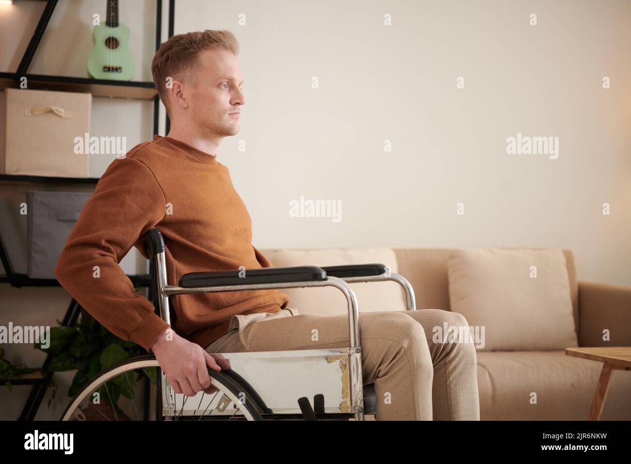 Serious young man with disability moving around house in wheelchair ...
