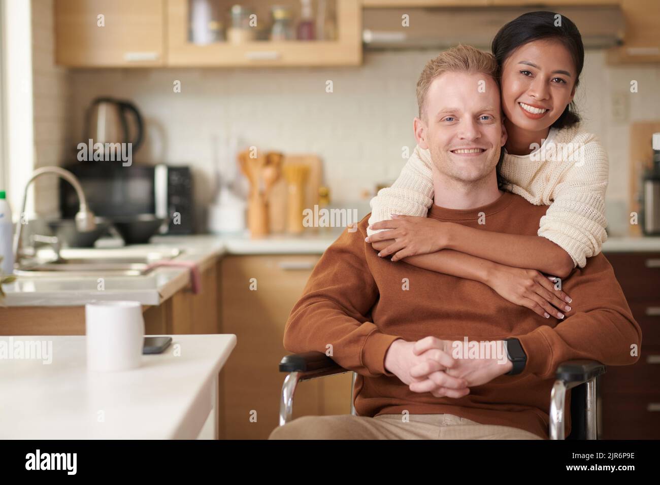 Portrait of smiling young woman hugging her boyfriend with disability Stock Photo - Alamy