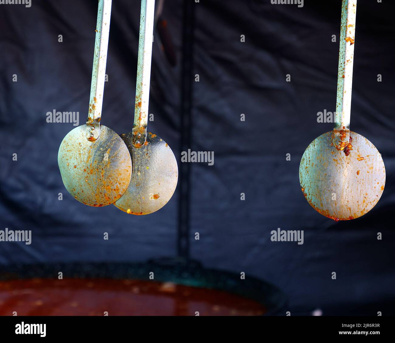 Large kitchen spoons, used in cooking, seen hanging down against a dark ...