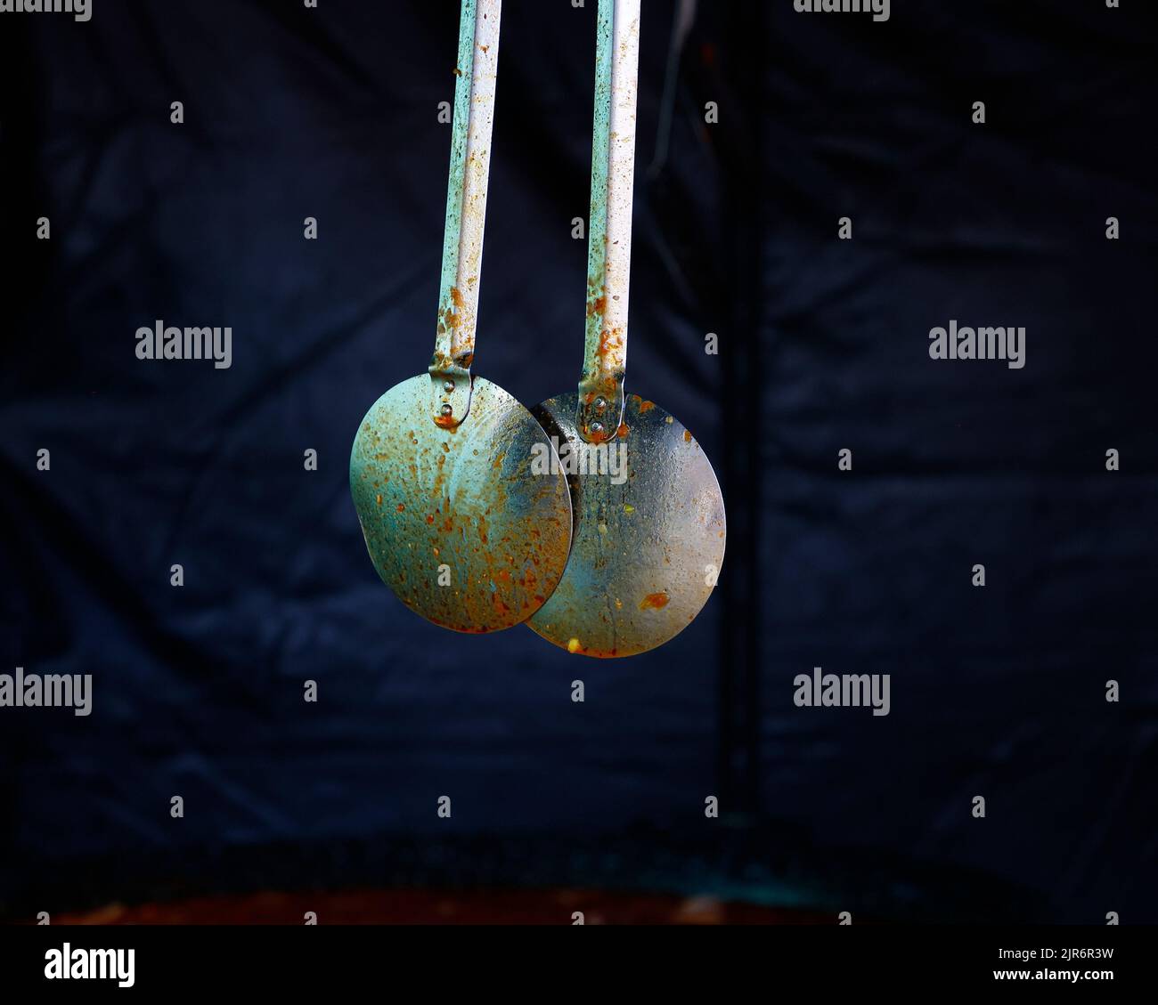Large kitchen spoons, used in cooking, seen hanging down against a dark ...