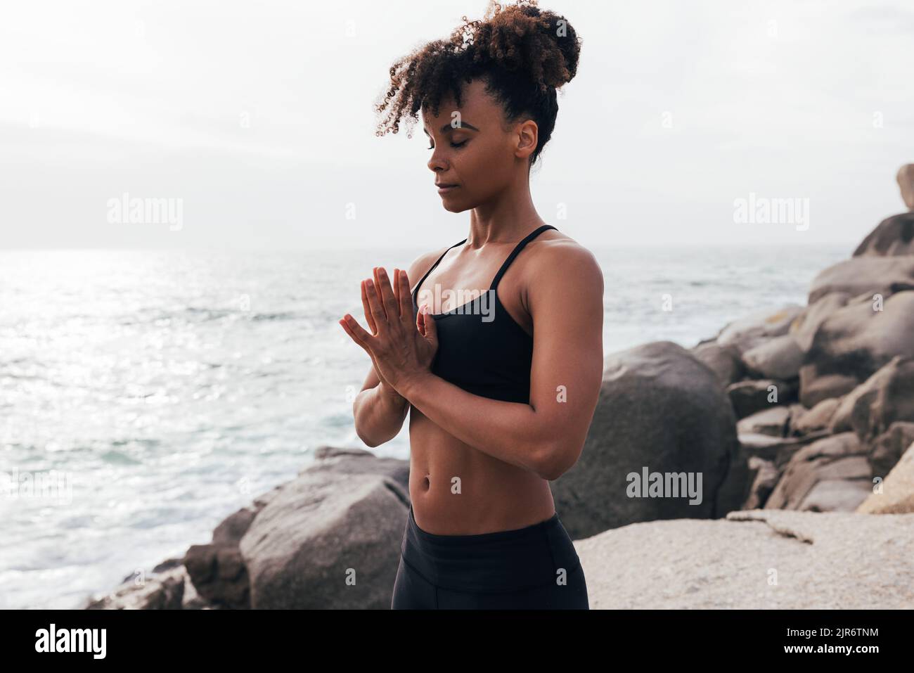 Young woman with folded hands standing at sunset by ocean. Female ...