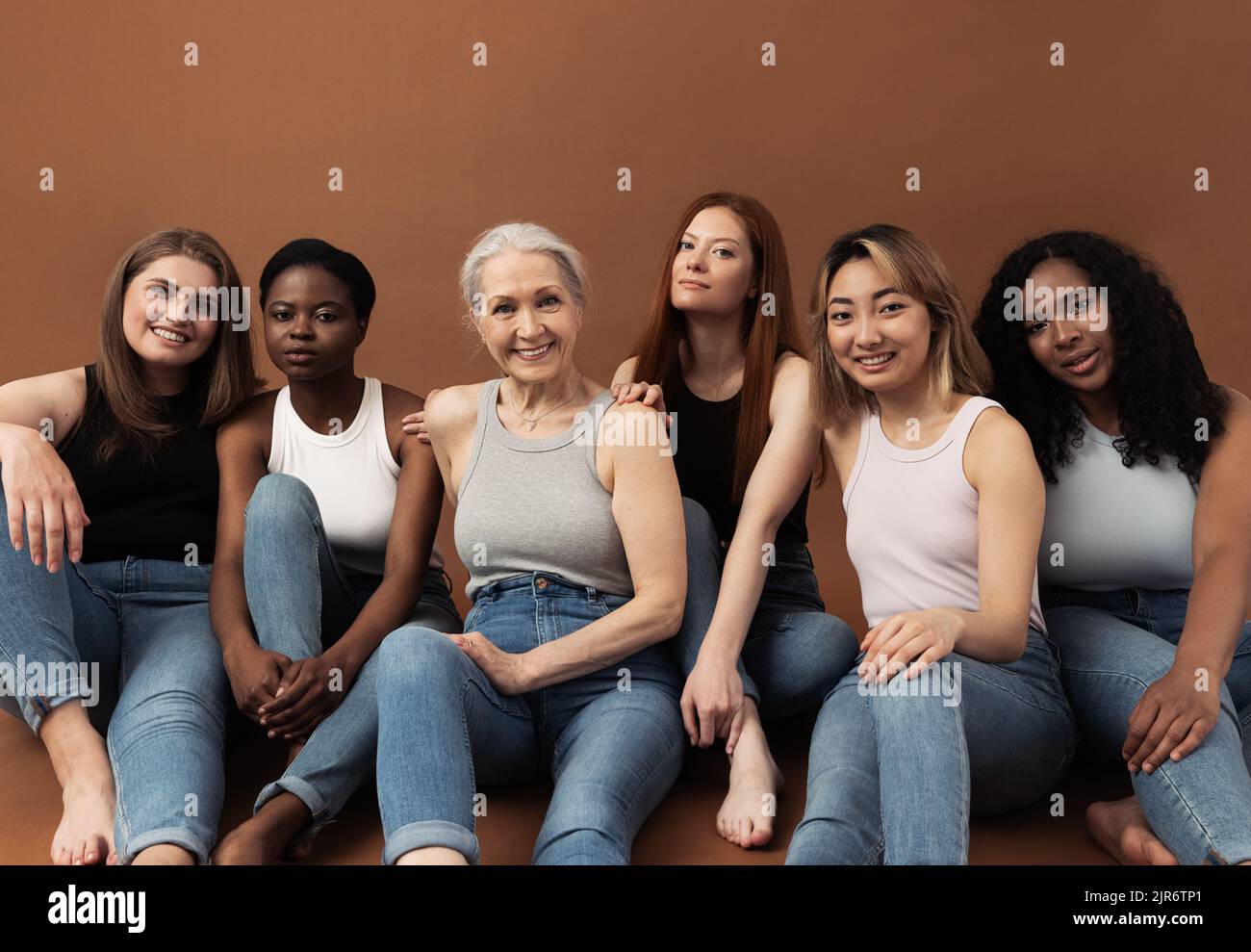 Group of six different women in casuals sitting together on brown ...