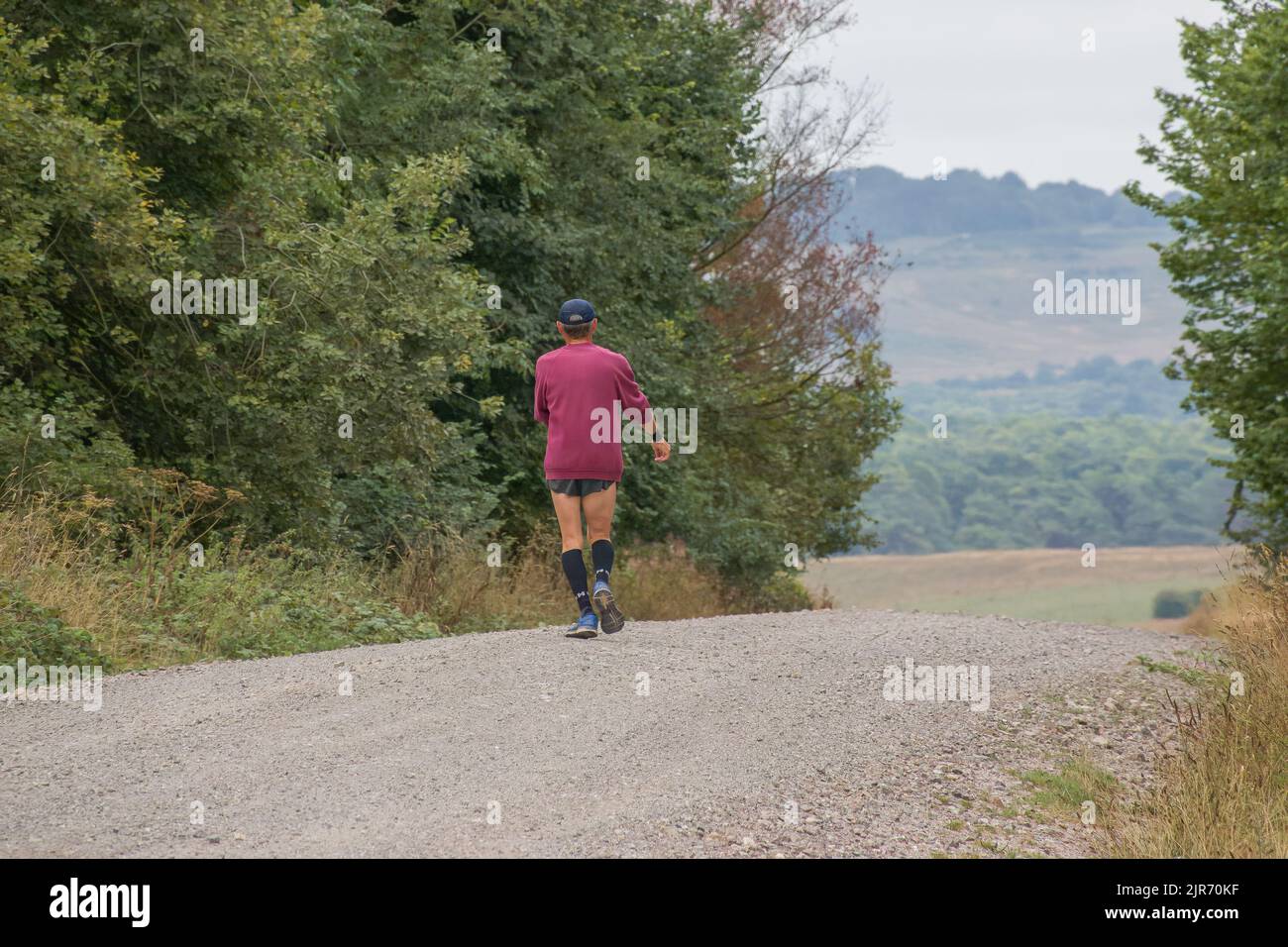 a lone man in a purple top, jogging along an unmade track road, hiking ...